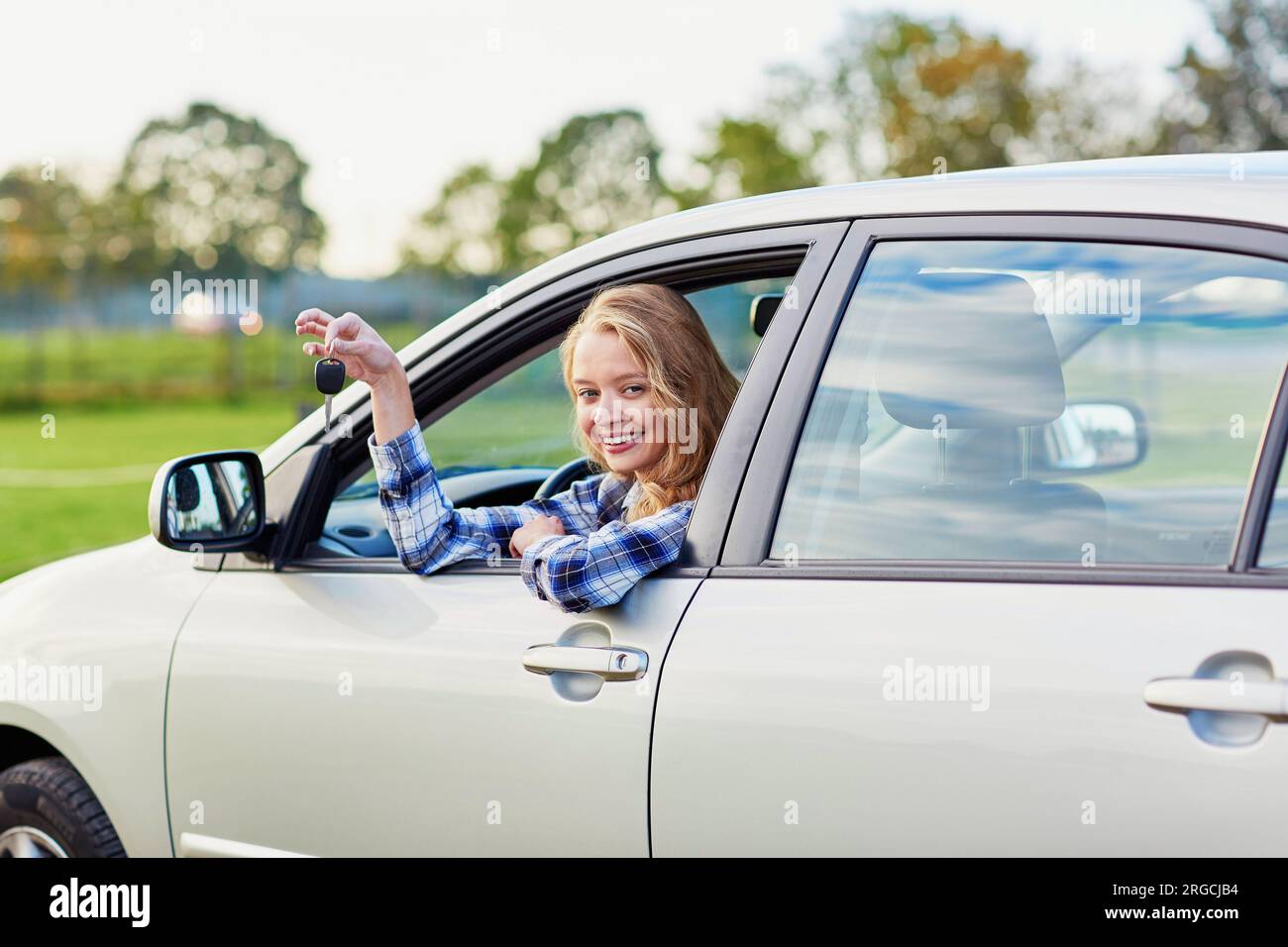Beautiful young driver looking out of the car window holding a key ...