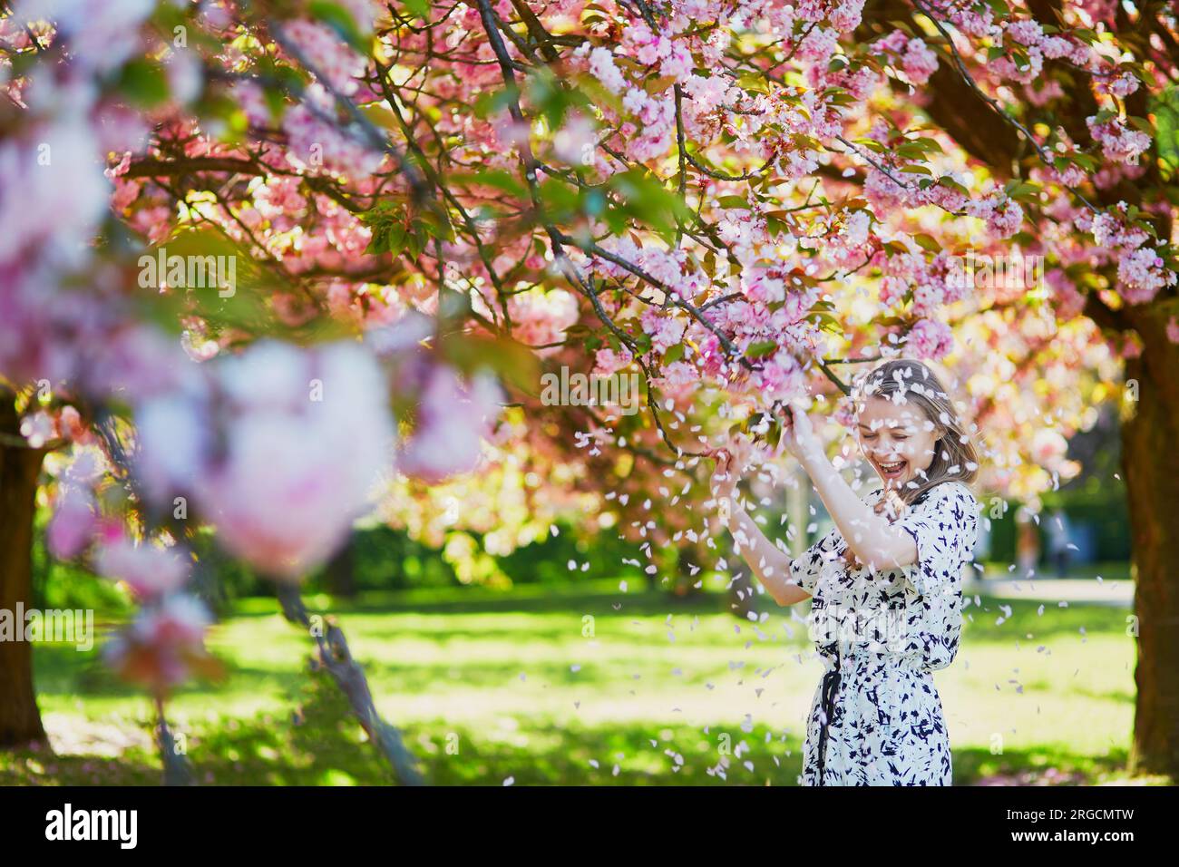 Beautiful young woman enjoying sunny day in park during cherry blossom ...