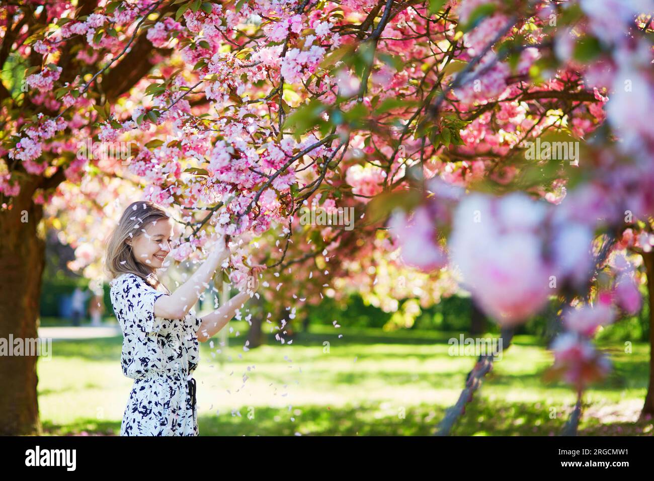 Beautiful young woman enjoying sunny day in park during cherry blossom ...