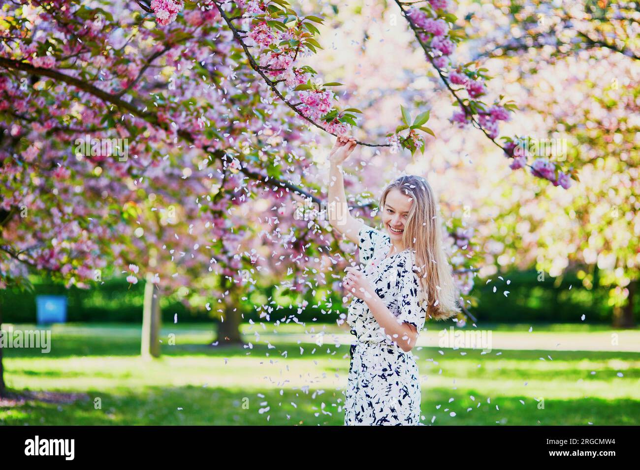 Beautiful young woman enjoying sunny day in park during cherry blossom ...