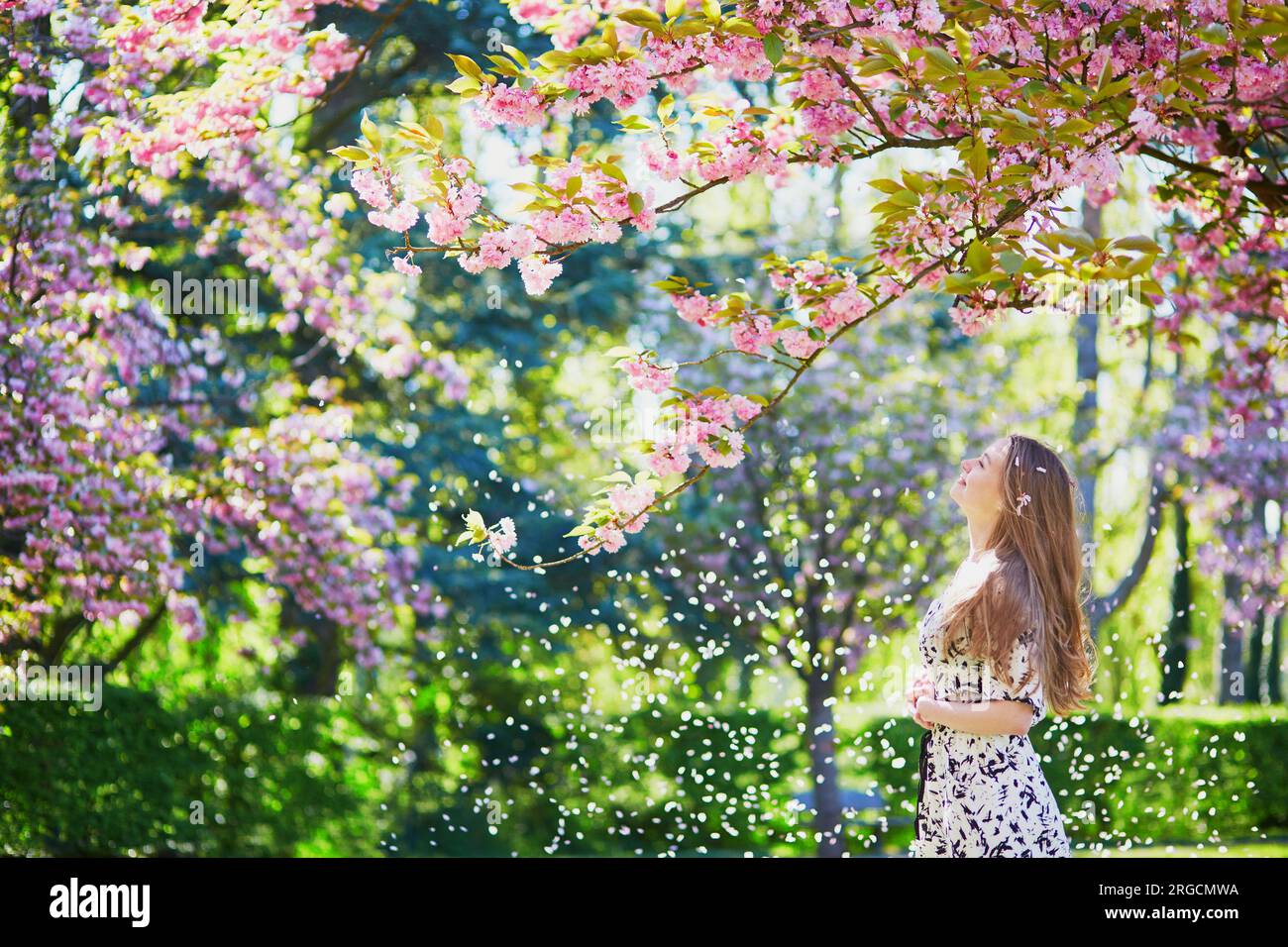 Beautiful young woman enjoying sunny day in park during cherry blossom ...