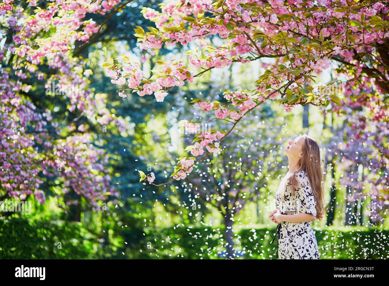 Beautiful young woman enjoying sunny day in park during cherry blossom ...