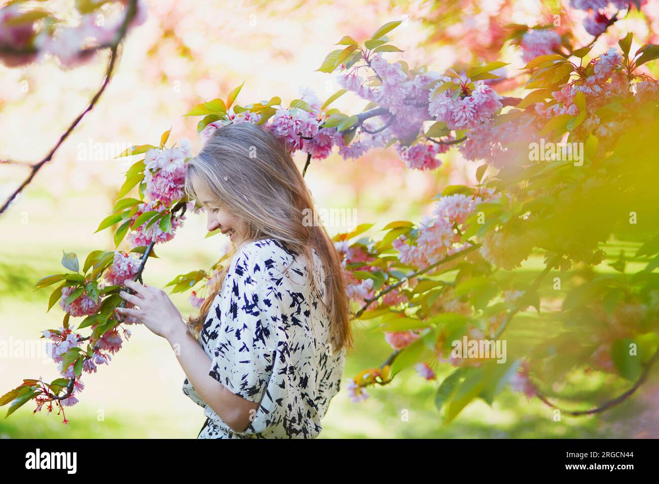 Beautiful young woman enjoying sunny day in park during cherry blossom ...