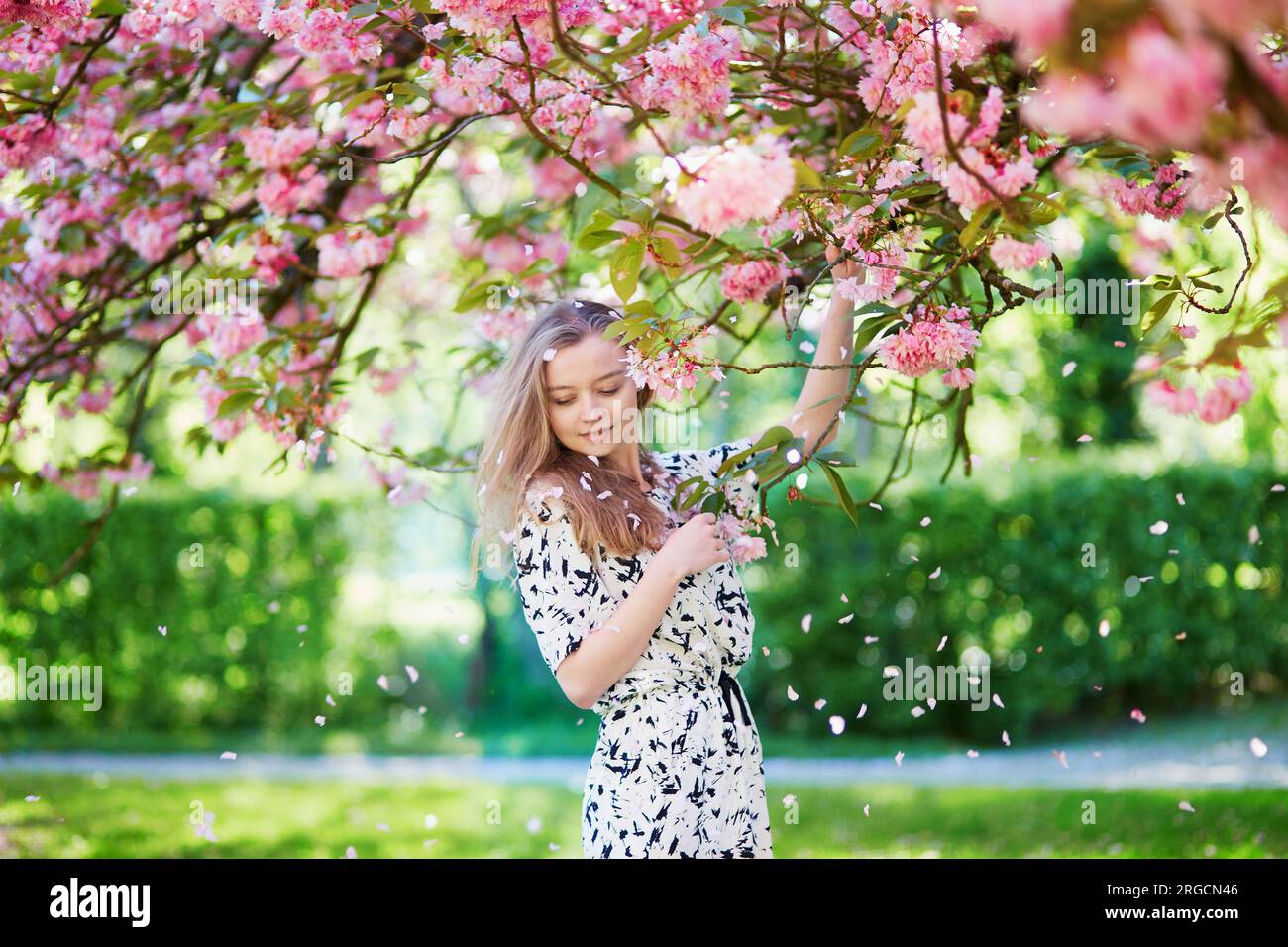 Beautiful young woman enjoying sunny day in park during cherry blossom ...