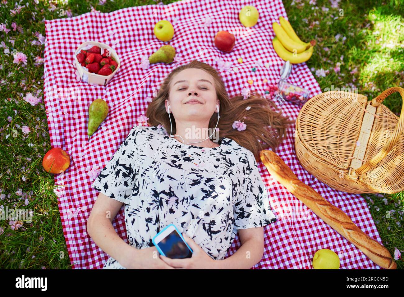 Beautiful young woman having picnic in parc, lying on her back with ...