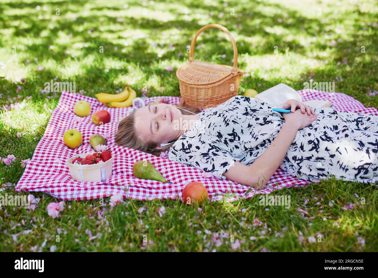 Beautiful young woman having picnic in parc, lying on her back with ...