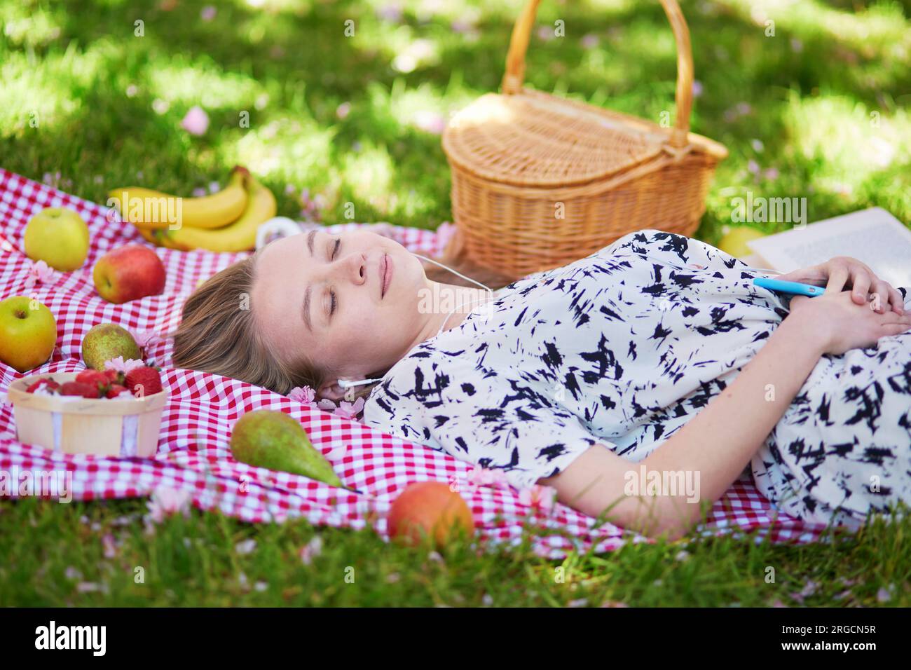 Beautiful young woman having picnic in parc, lying on her back with ...