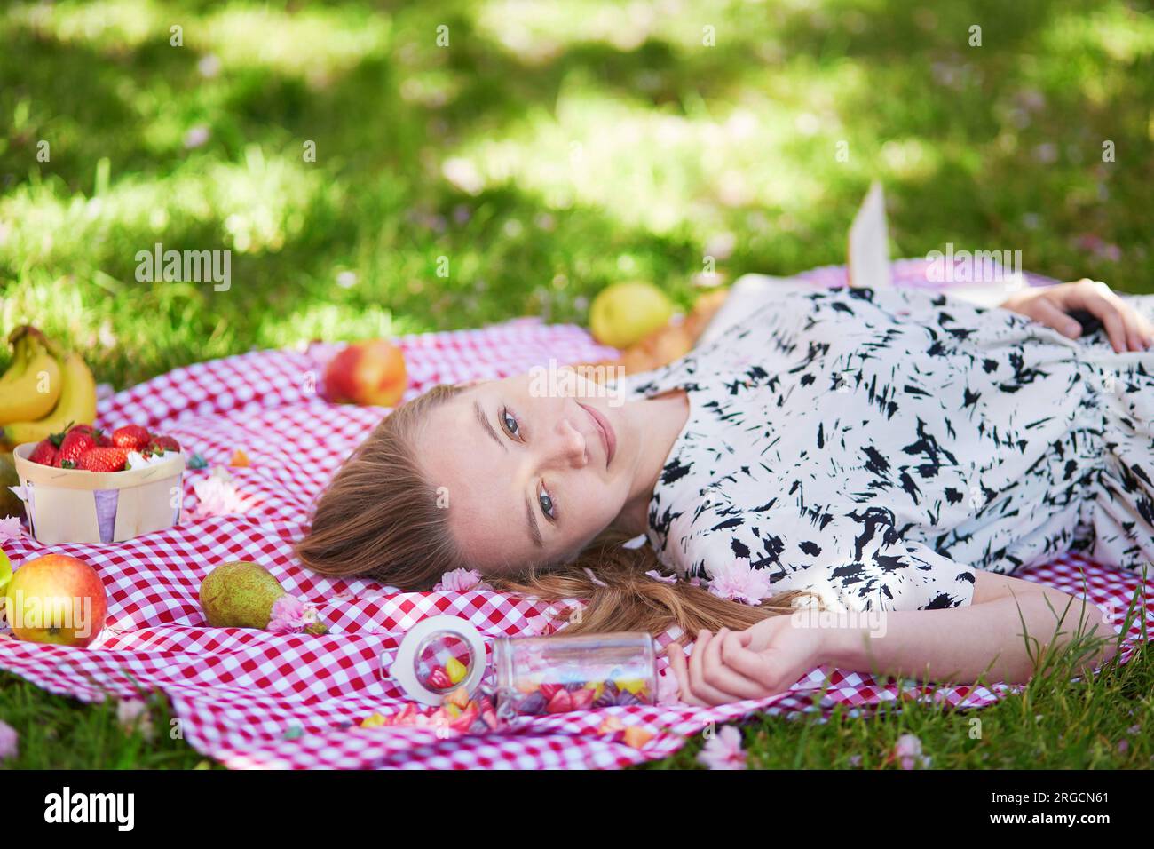 Beautiful young woman having picnic in parc, lying on her back with ...