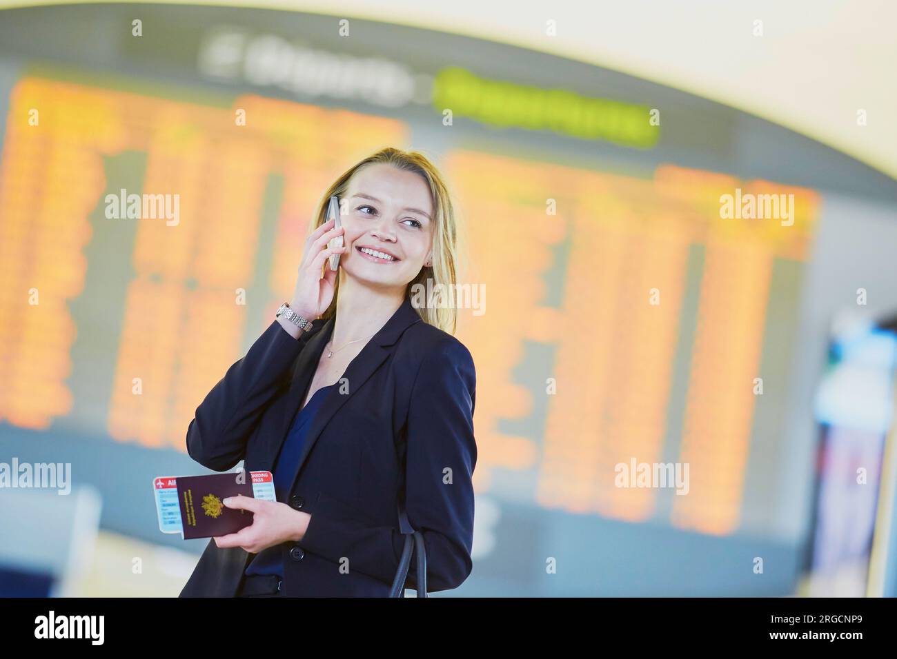 Young elegant business woman holding passport and boarding pass, talking on the mobile phone ...
