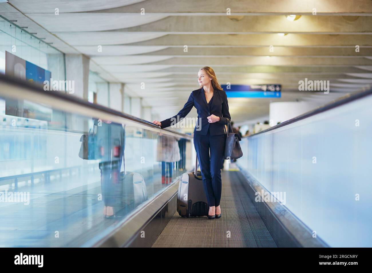 Young elegant business woman with hand luggage on travelator on ...
