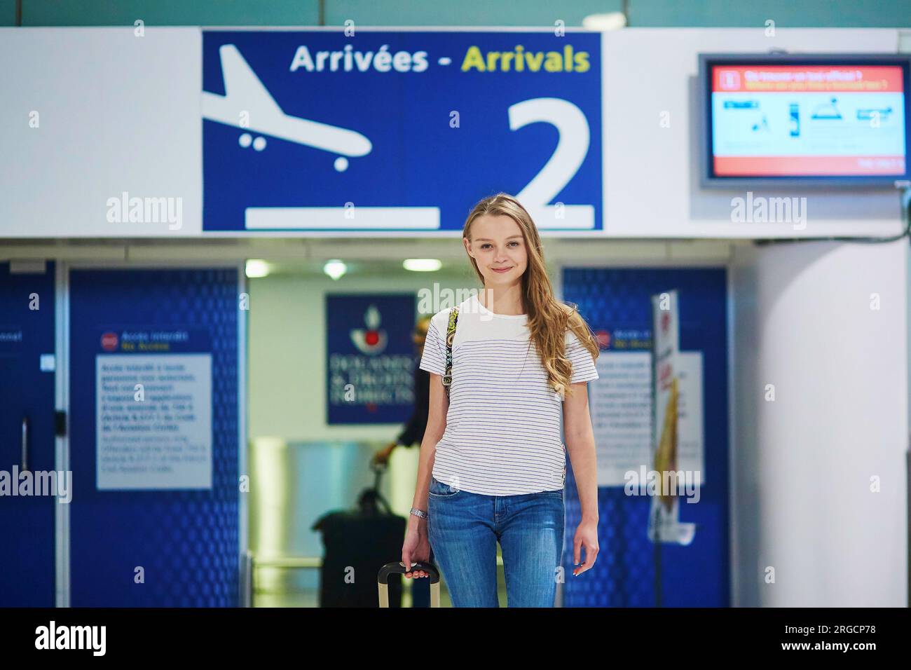 Beautiful young tourist girl with backpack and carry on luggage in international airport, at ...