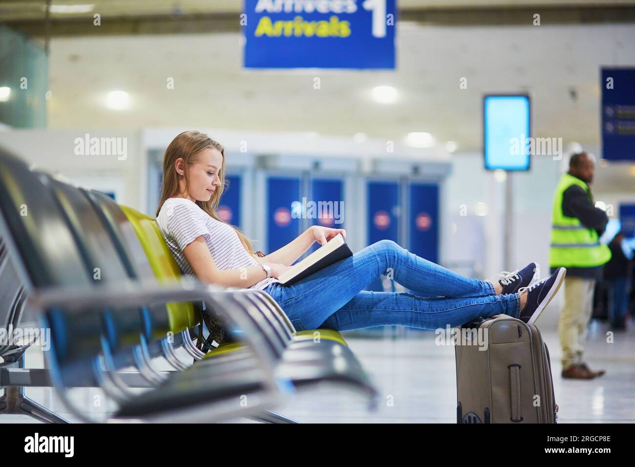 Young traveler with carry on luggage in international airport reading a ...