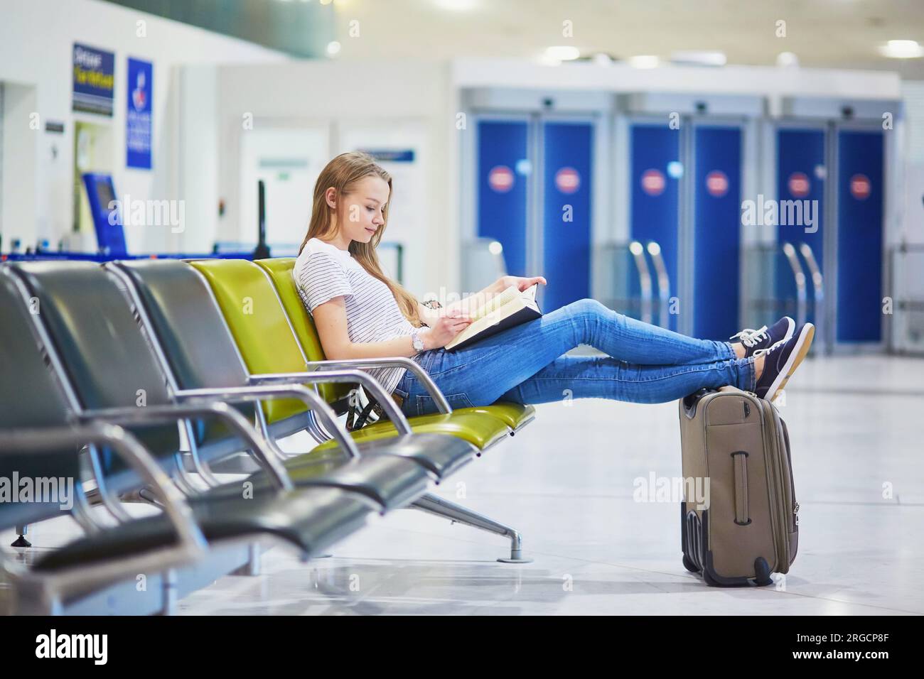 Young woman in international airport reading a book while waiting for ...