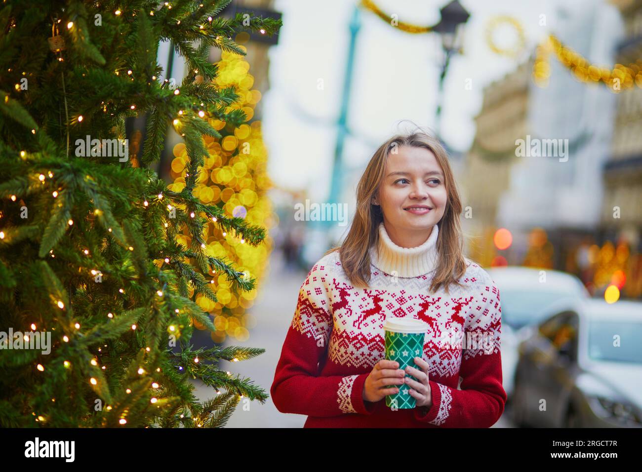 Happy young girl in holiday sweater walking with hot drink to go on a ...