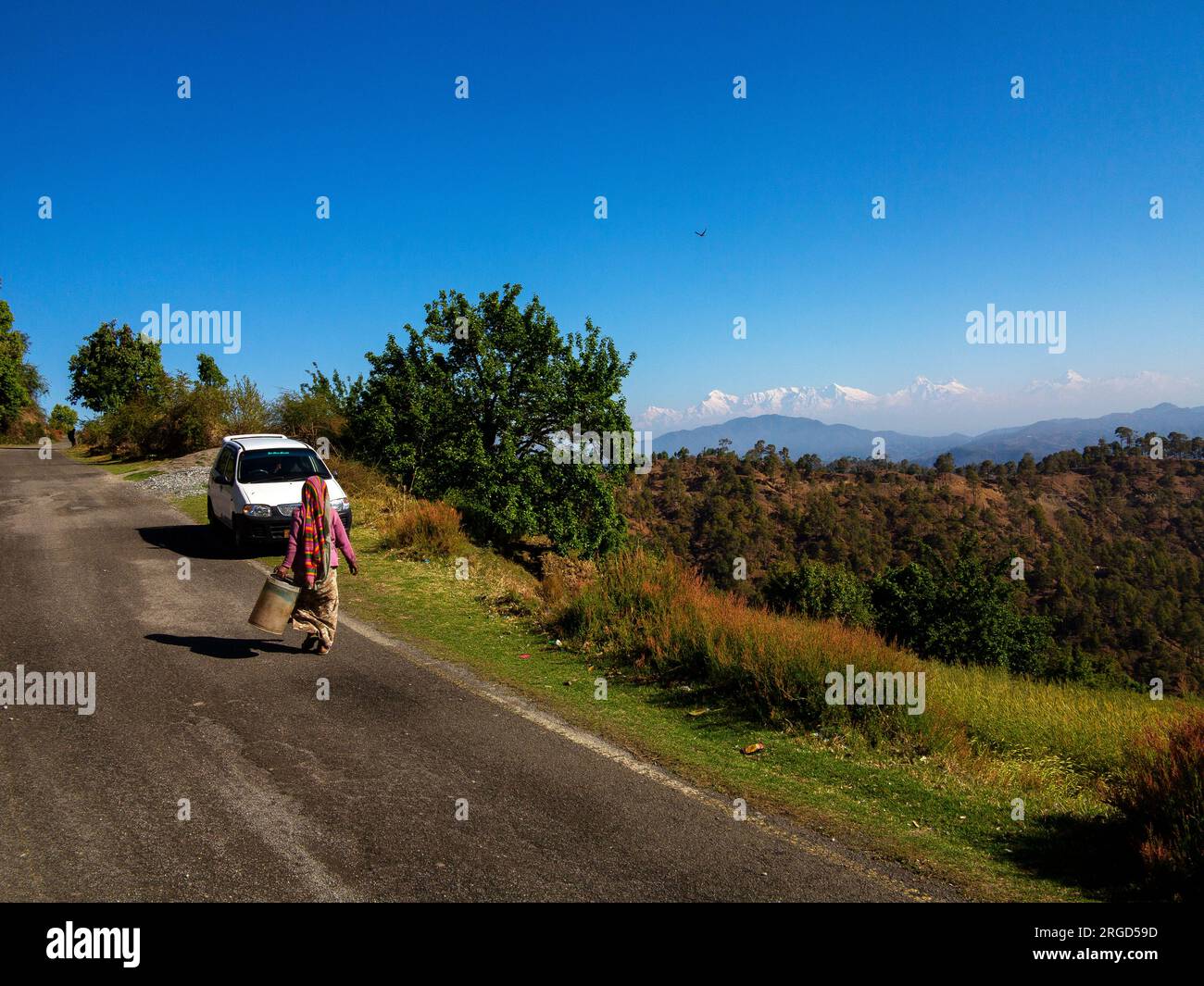 Indian woman walking on the road, with the Himalayas on the distance as ...
