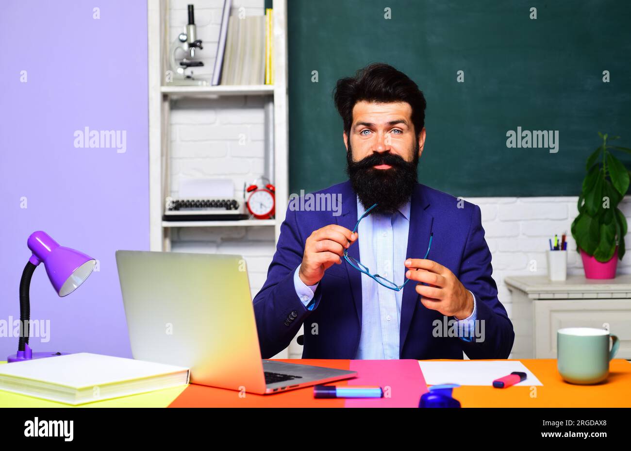 Serious bearded teacher working with laptop computer in classroom ...