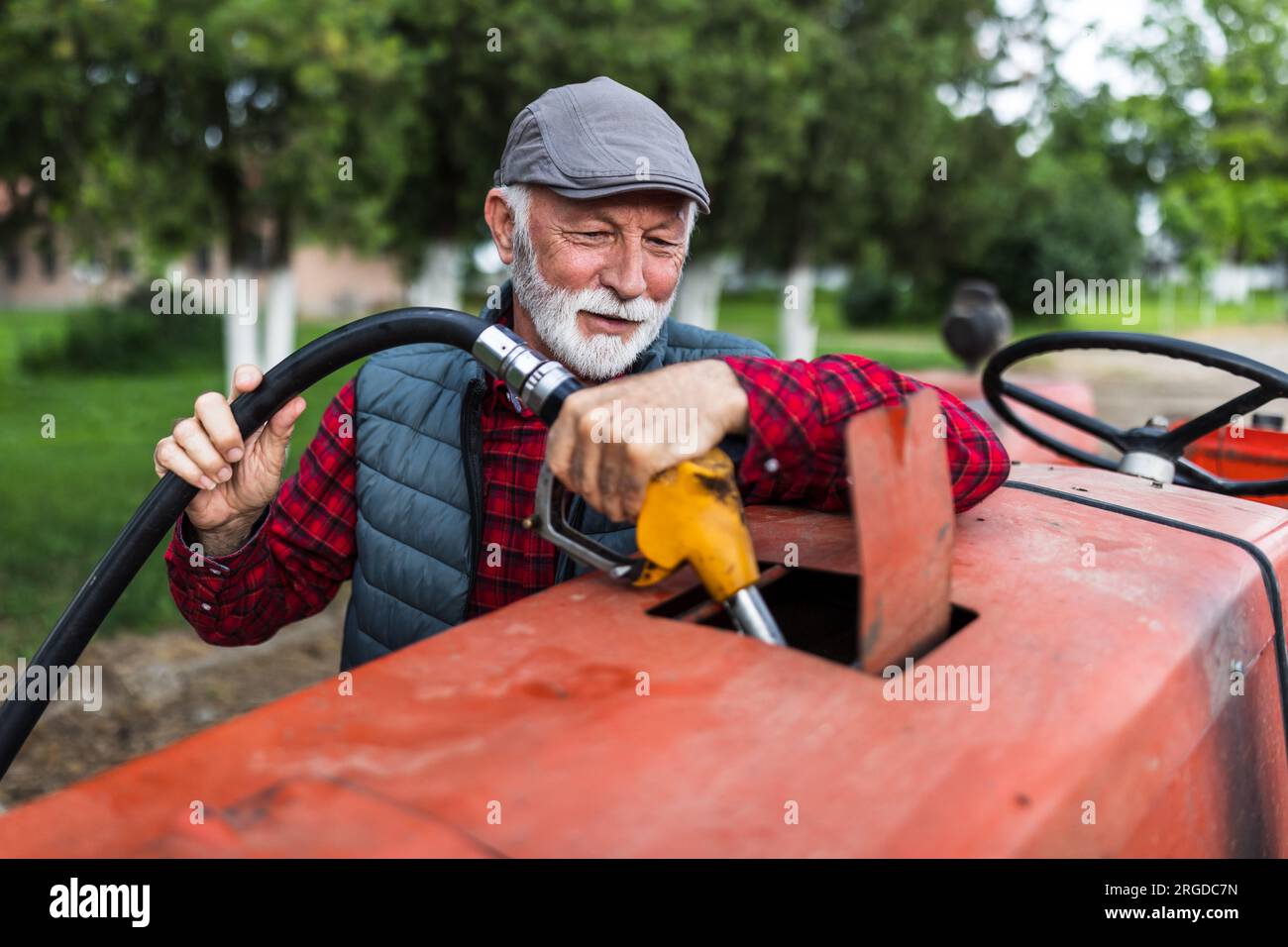 Senior farmer holding fuel pistol and refilling reservoir of tractor on ...