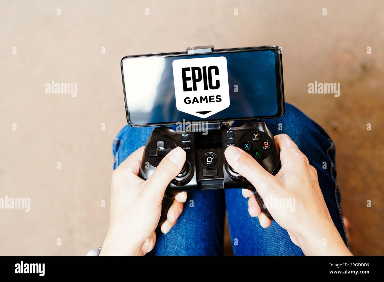 In this photo illustration, a person playing on a joystick and the Epic Games logo displayed on ...