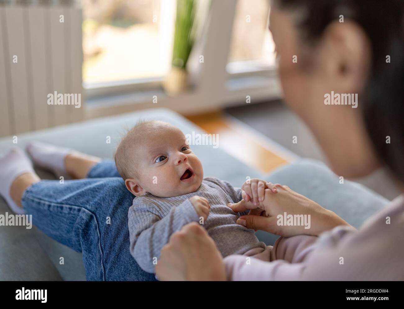 Young mother sitting on sofa at home and holding cute smiling newborn ...