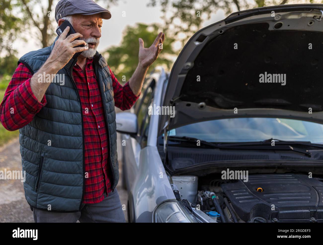 Senior man standing beside car with open hood and talking on mobile ...
