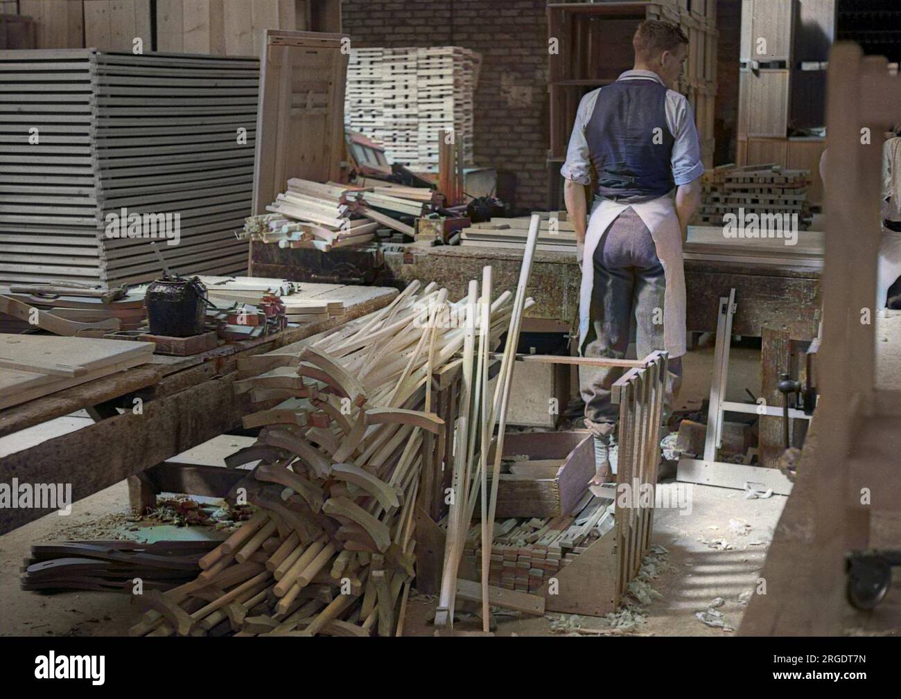Man at a workbench in a timber workshop. A pile of newly made crutches ...