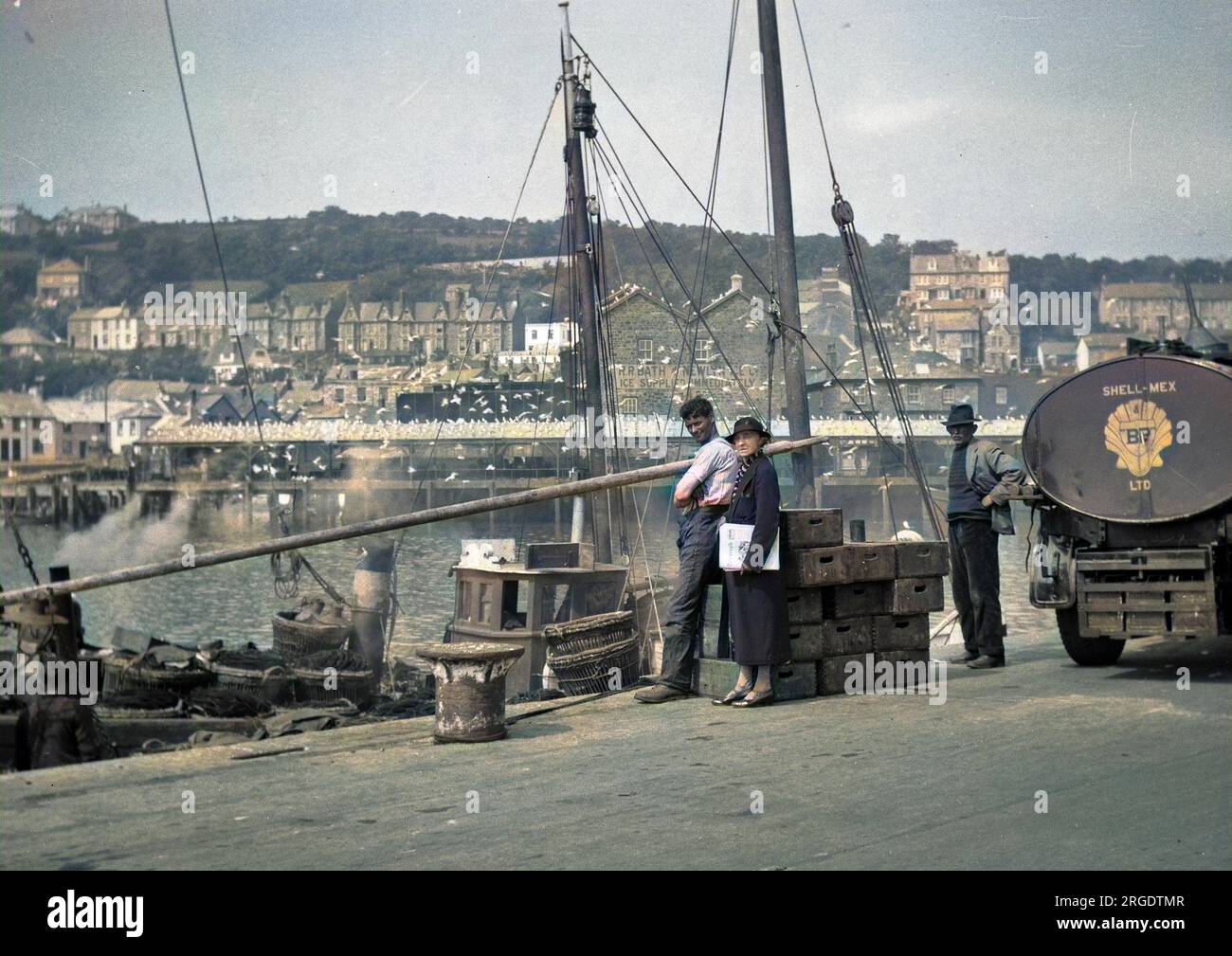 A harbour scene with fishing boats and seagulls. A Shell-Mex BP vehicle ...