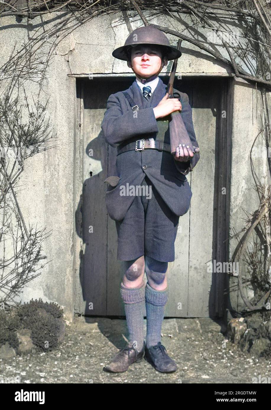 A boy in a tin helmet with a rifle on his shoulder, playing at being on ...