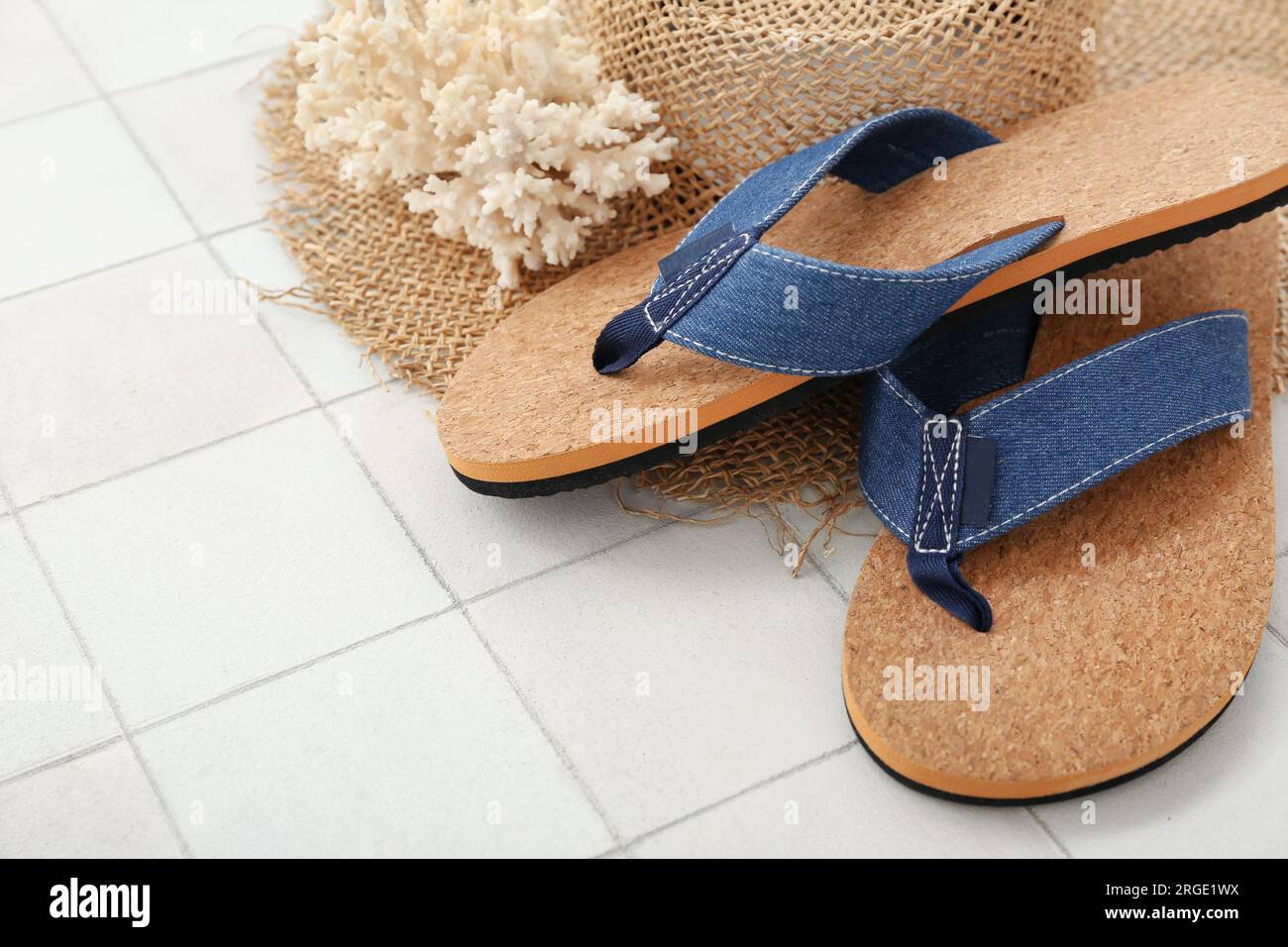 Pair of flip flops with straw hat and coral on white tile background ...