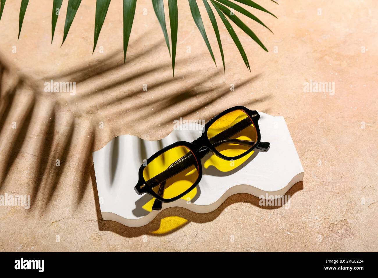 Decorative podium with stylish sunglasses and palm leaf on orange ...