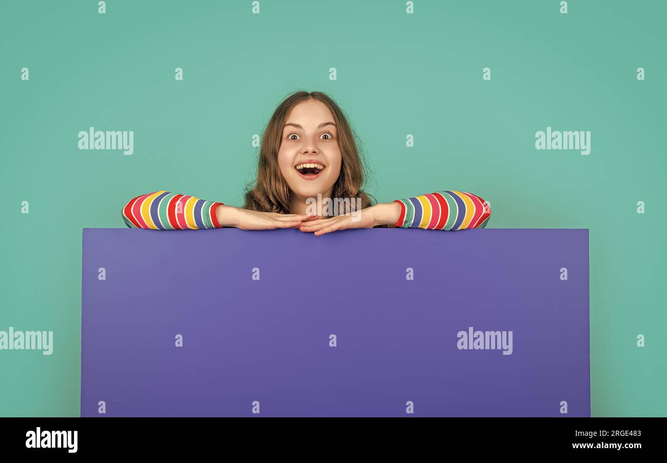 happy shocked child behind blank blue paper with copy space for ...