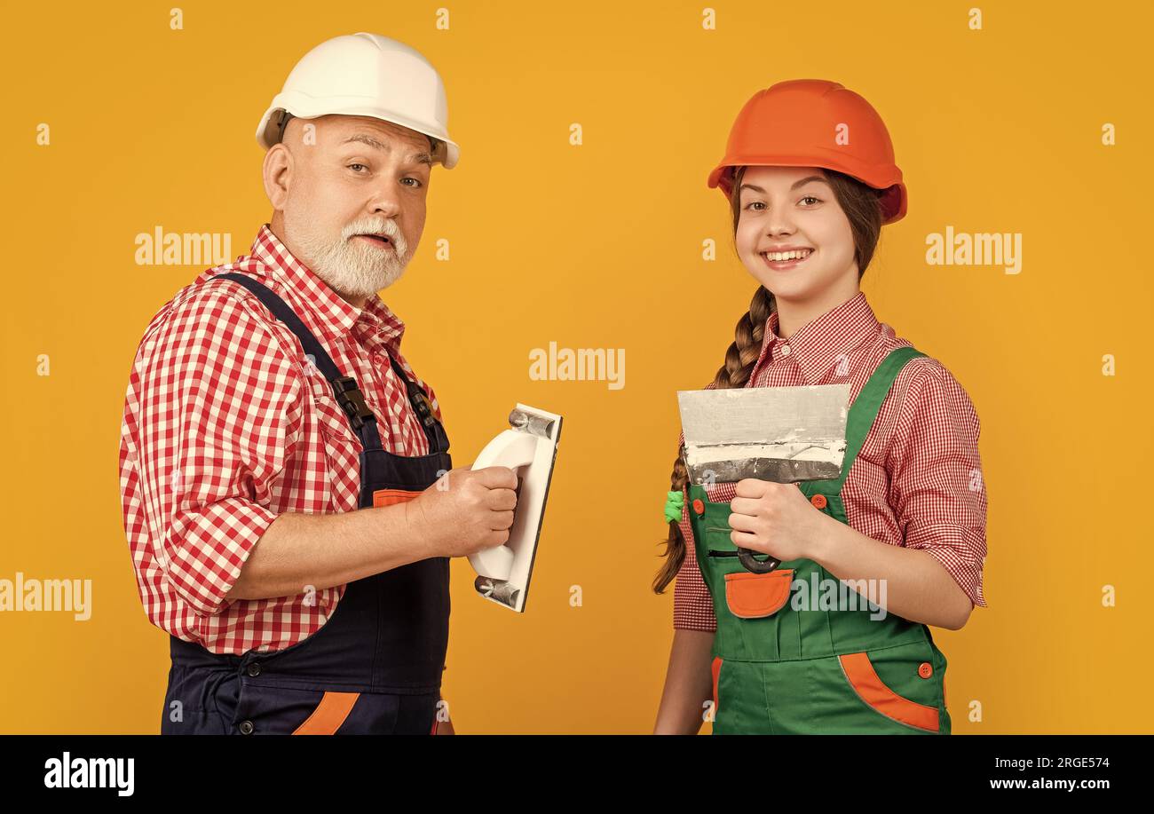 happy child and grandfather plasterer in hard hat on yellow background ...
