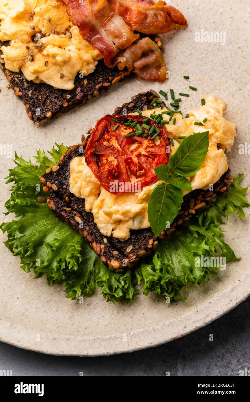 Scrambled eggs with bacon and tomato on toasted grain bread Stock Photo ...