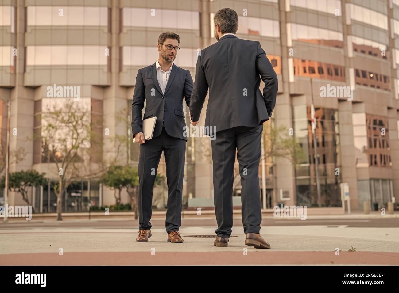 full length of two business men in suit are handshaking in agreement ...