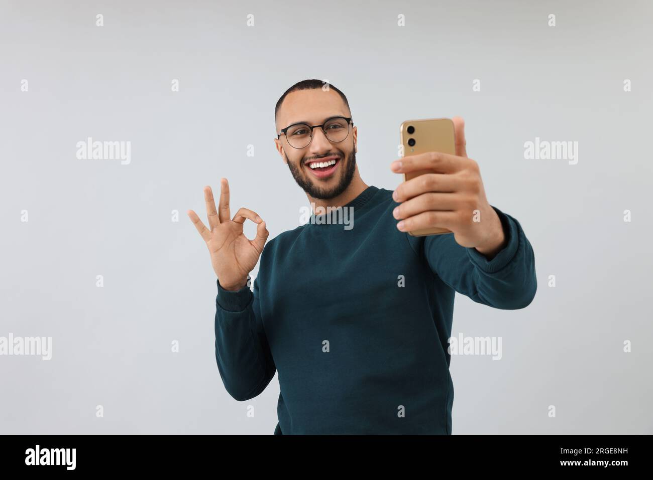 Smiling young man taking selfie with smartphone and showing OK gesture ...