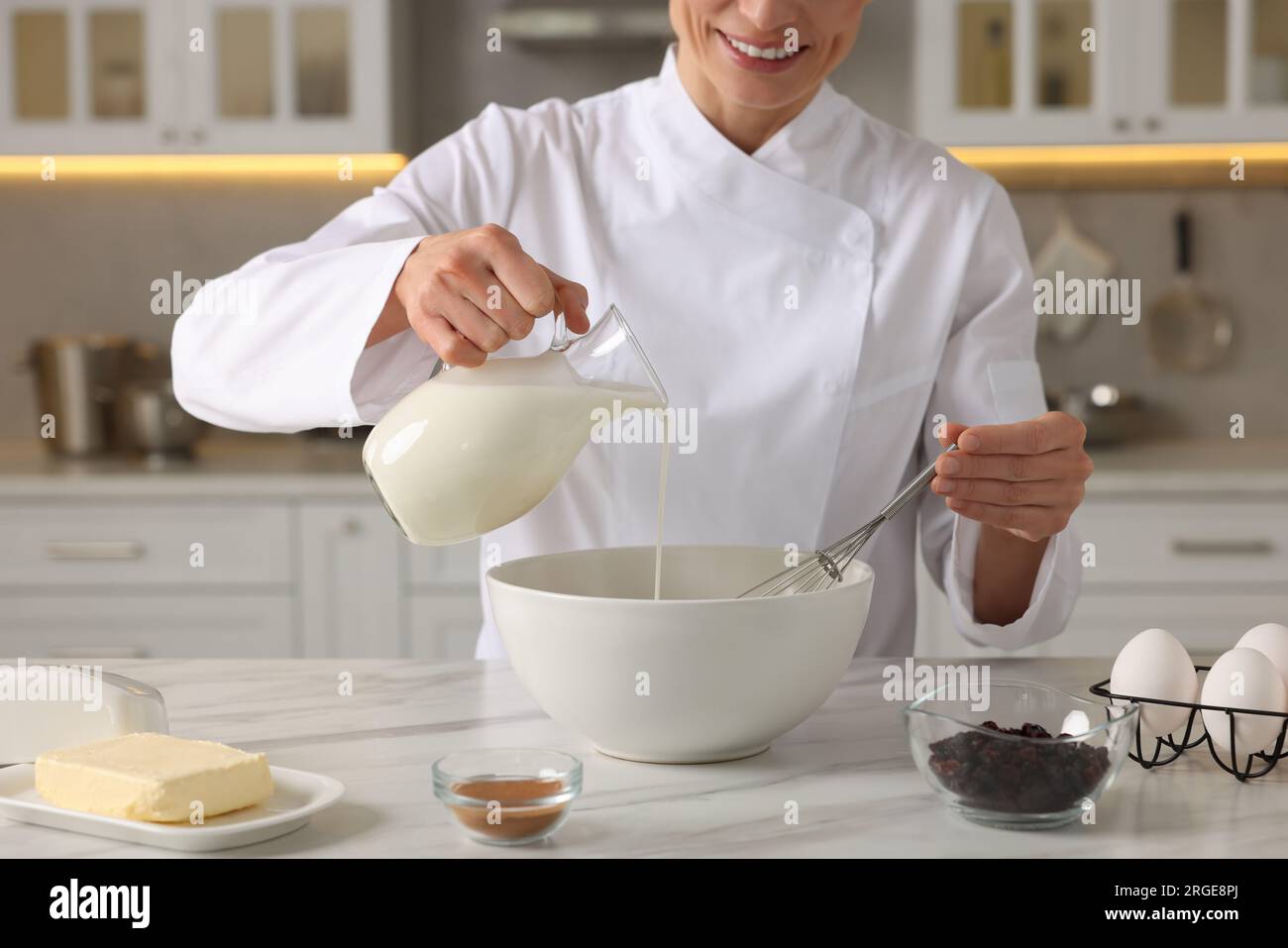 Professional chef adding milk into dough at white marble table indoors ...