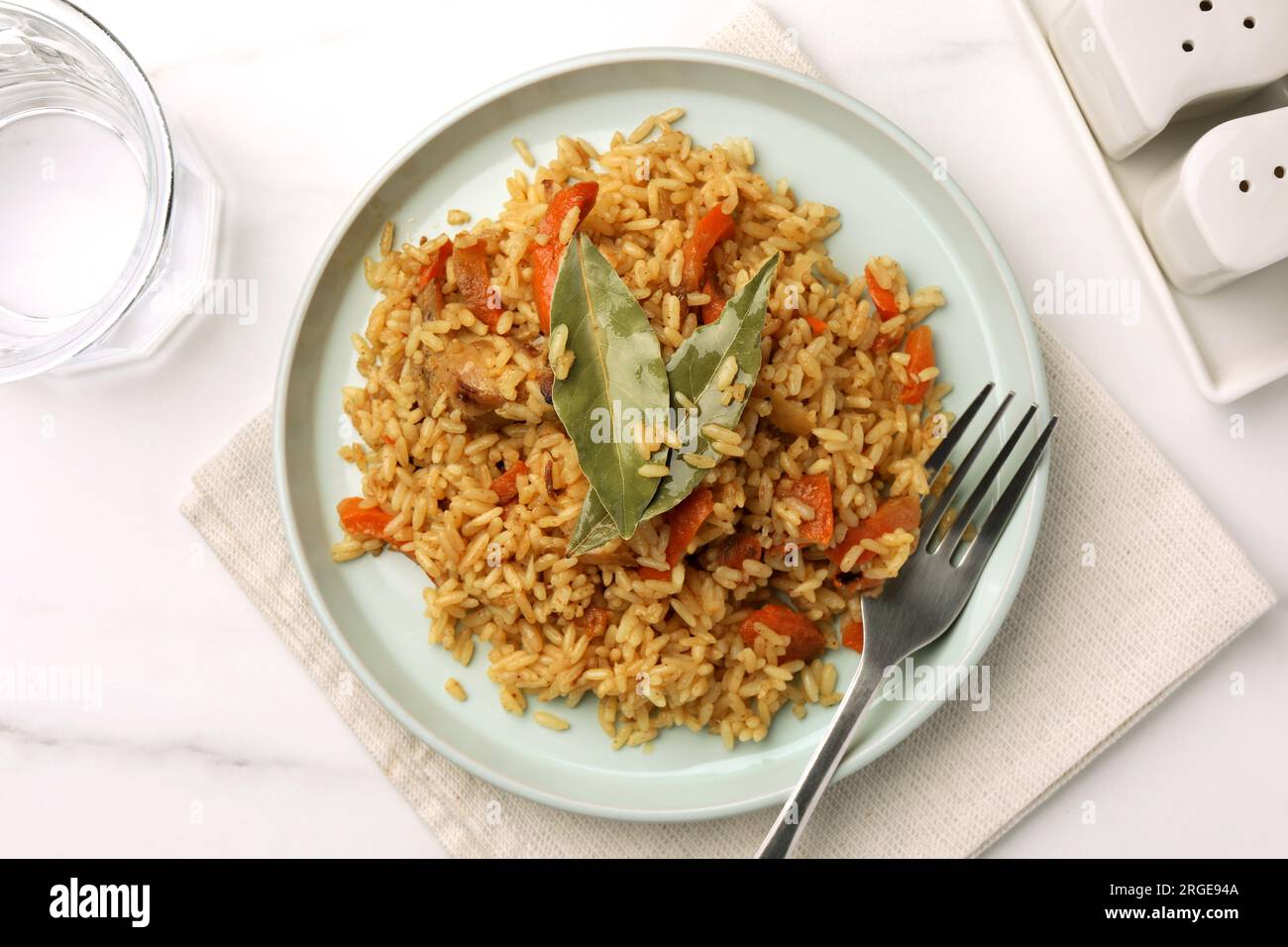 Delicious pilaf, bay leaves, fork and glass of water on white table ...
