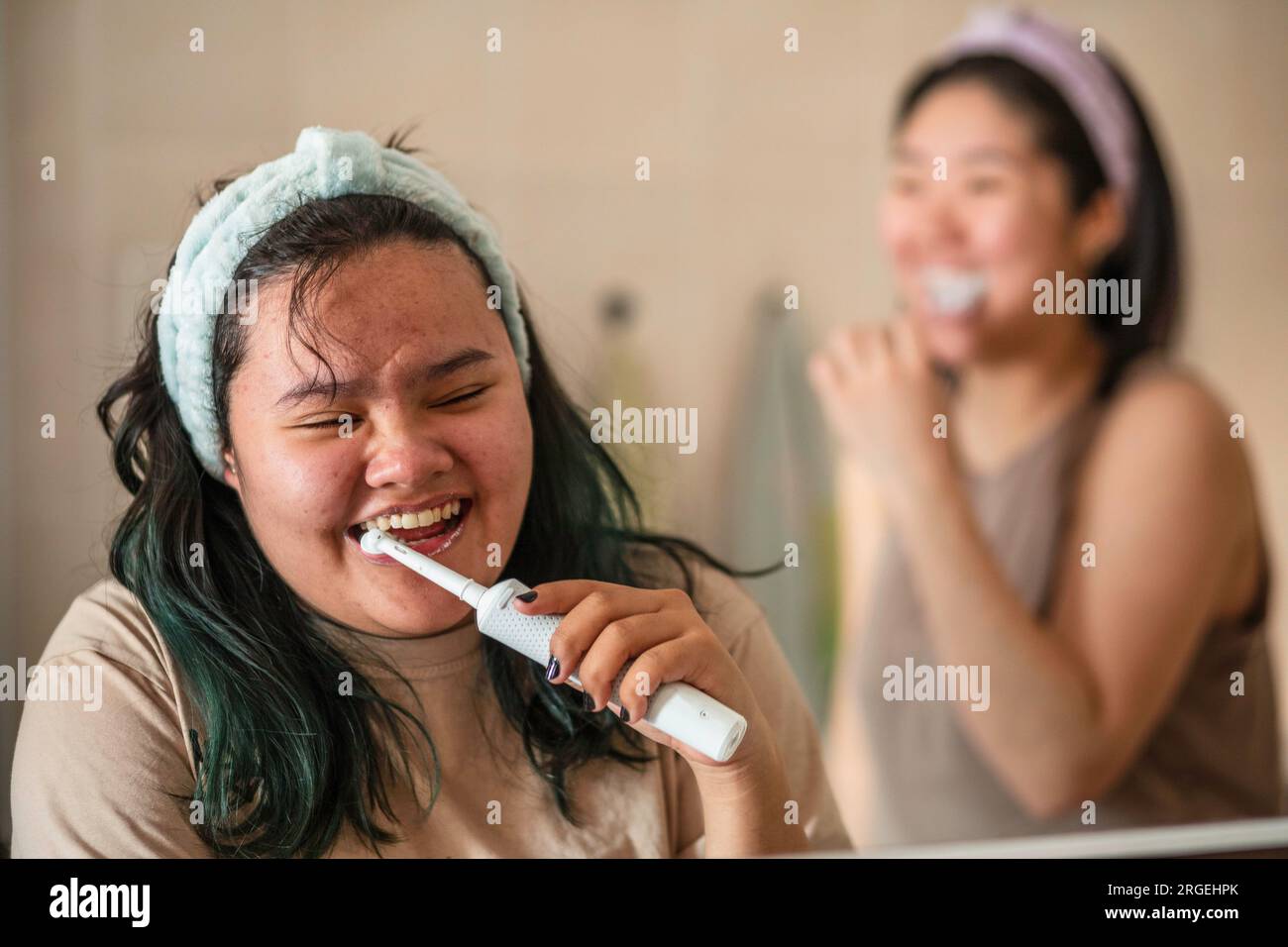 two asian girls in hairbands brushing teeth laughing cheerfully in the ...