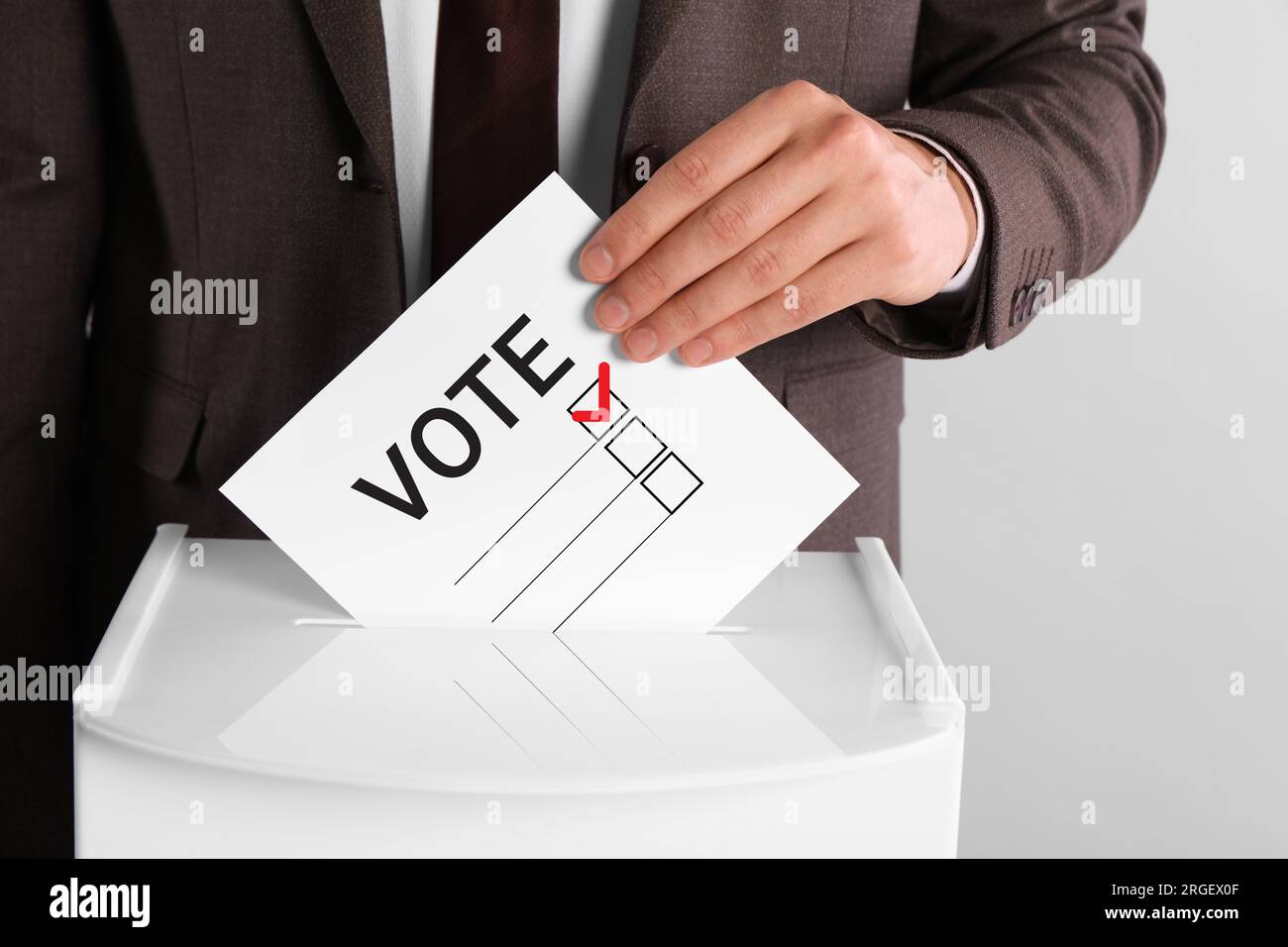 Man putting paper with word Vote and tick into ballot box on light grey ...