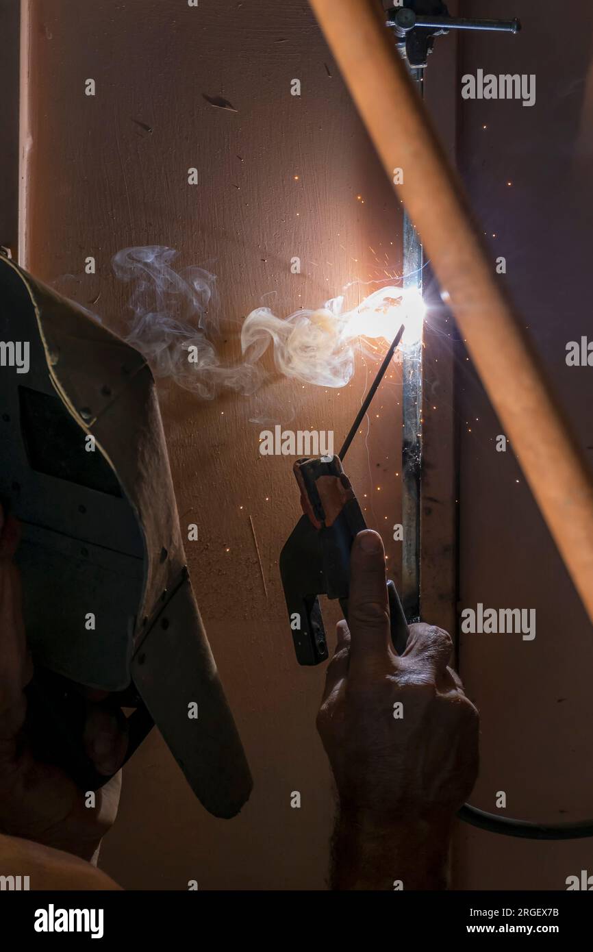 A man protected by a self-darkening mask welds an iron bolt to a trap ...