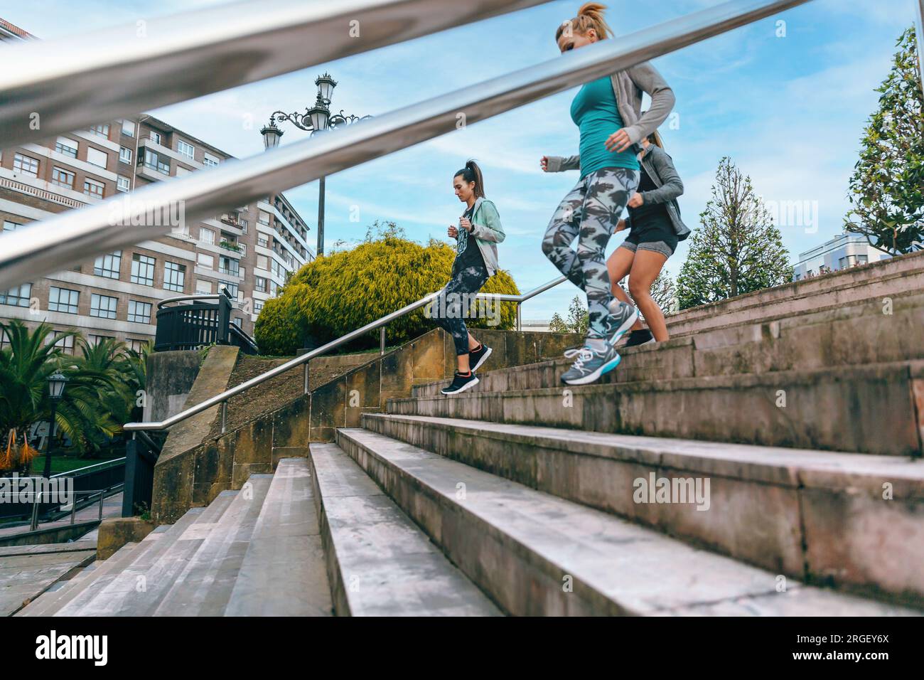 Group of happy young women friends training running down stairs in town ...