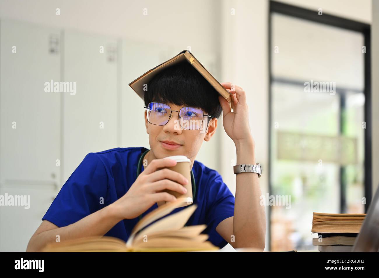 Medical student man wearing blue scrubs putting book on head and ...