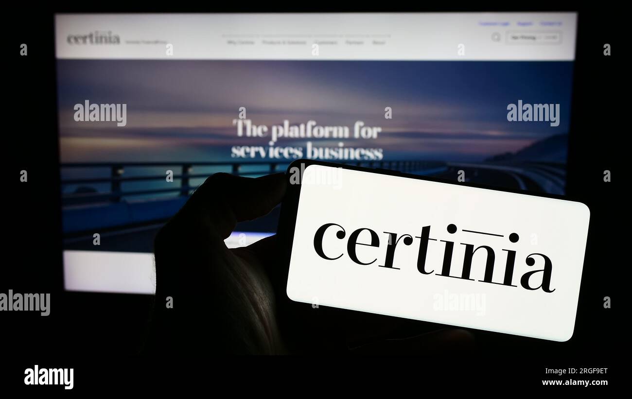 Person holding cellphone with logo of US software company Certinia Inc. on screen in front of ...