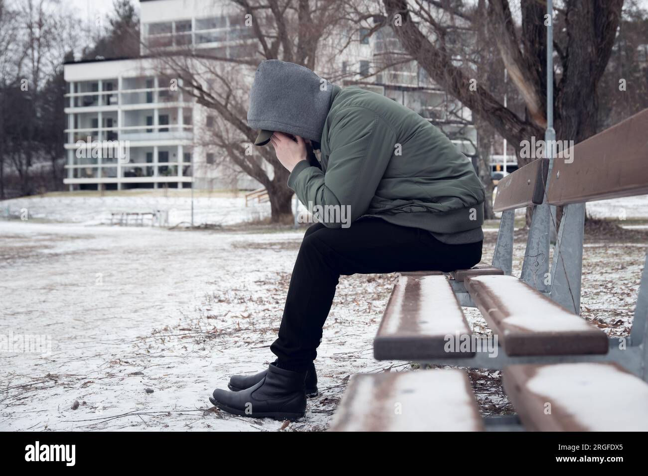 A Lonely and sad man sitting on a park bench in snowy winter scenery ...