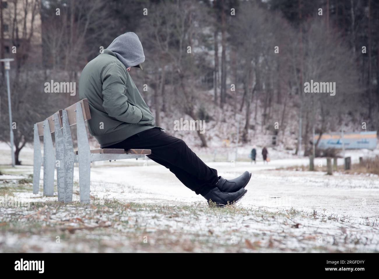 A Lonely man sitting on a park bench. Some snow on ground Stock Photo ...