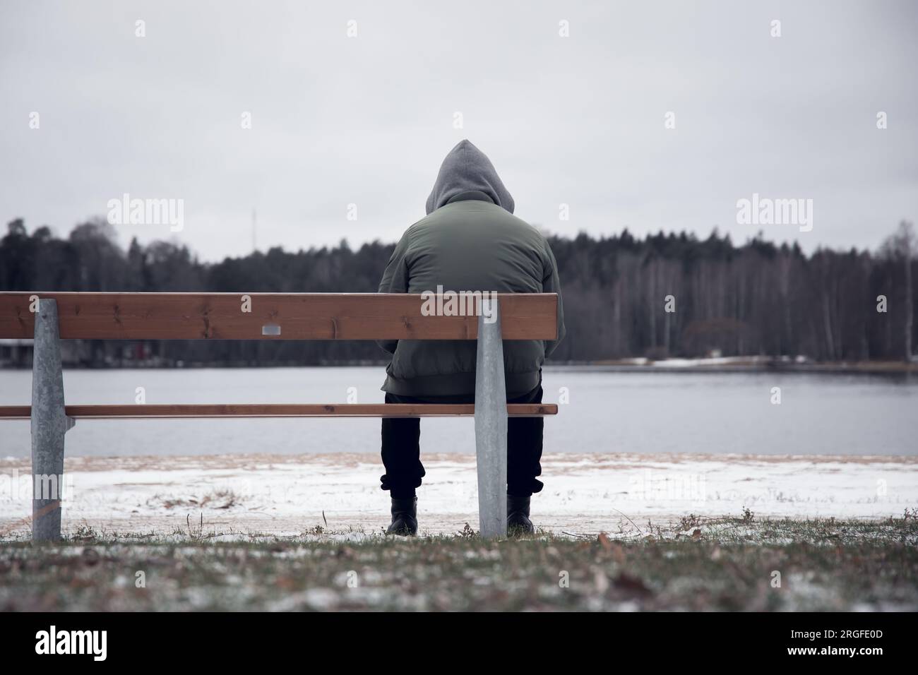A hooded man sitting alone on park bench Stock Photo - Alamy