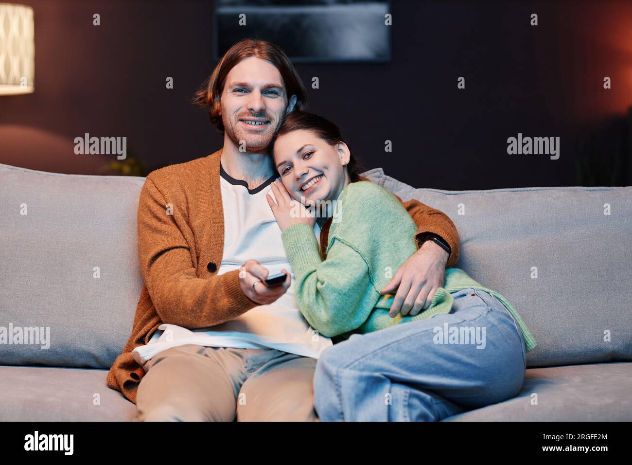 Front view portrait of smiling young couple watching TV at home and ...