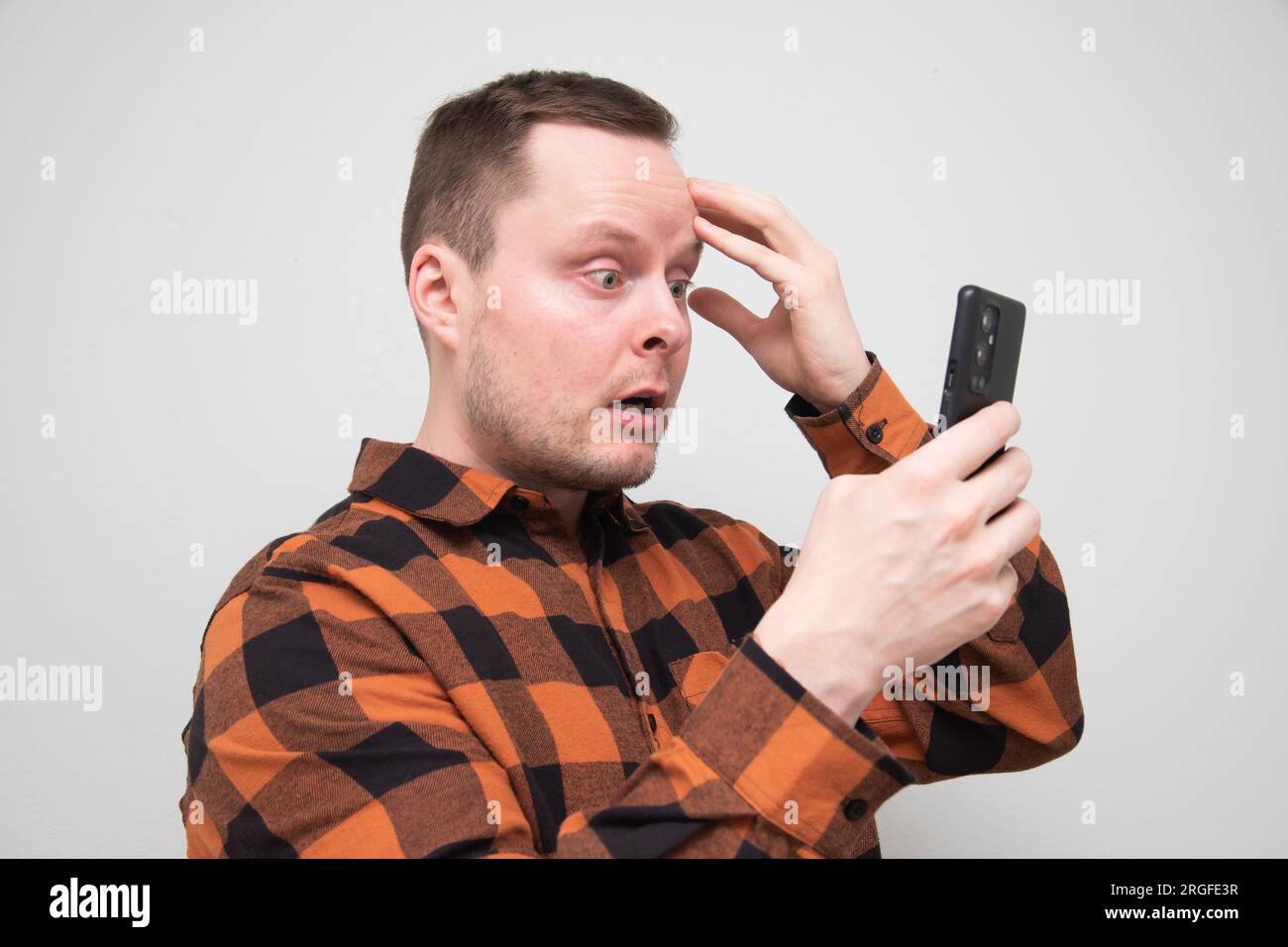 Man being shocked while looking at his smartphone on white background ...