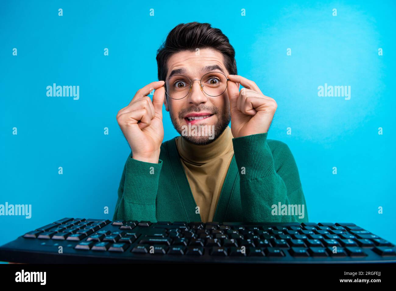 Photo of young nervous man nerd biting lips near computer keyboard wish ...