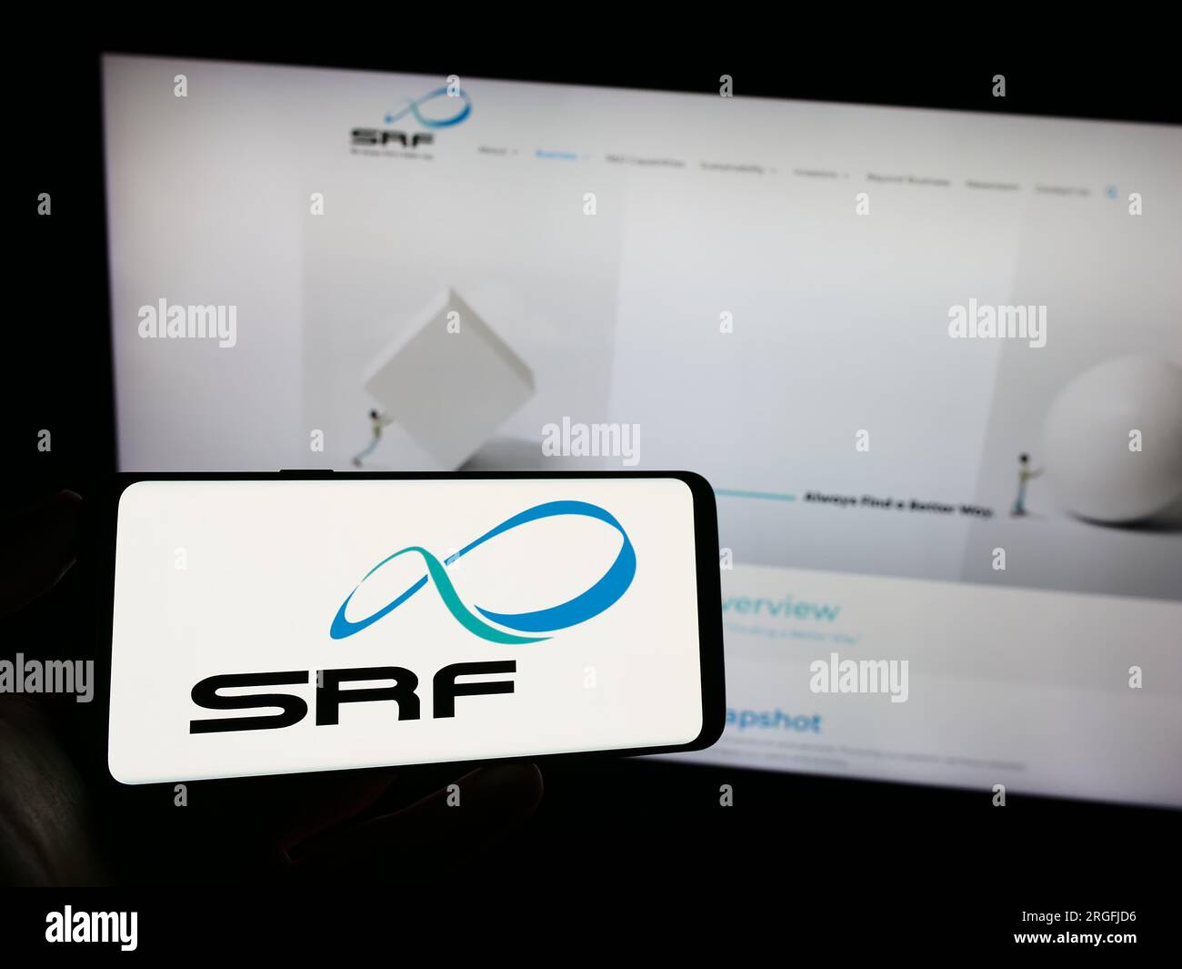 Person holding mobile phone with logo of Indian chemicals company SRF Limited on screen in front ...