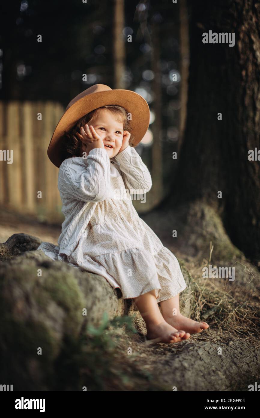 Excited little girl wearing hat, sitting bootless in the countryside ...